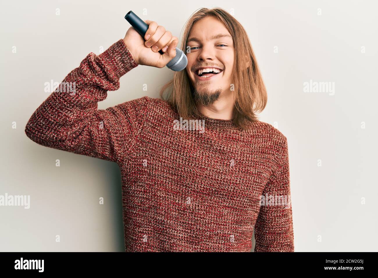 Handsome caucasian man with long hair singing song using microphone ...