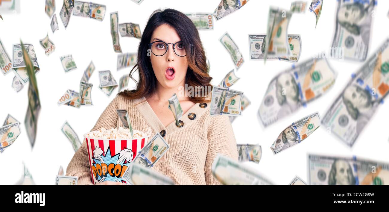 Beautiful young brunette woman eating popcorn scared and amazed with ...
