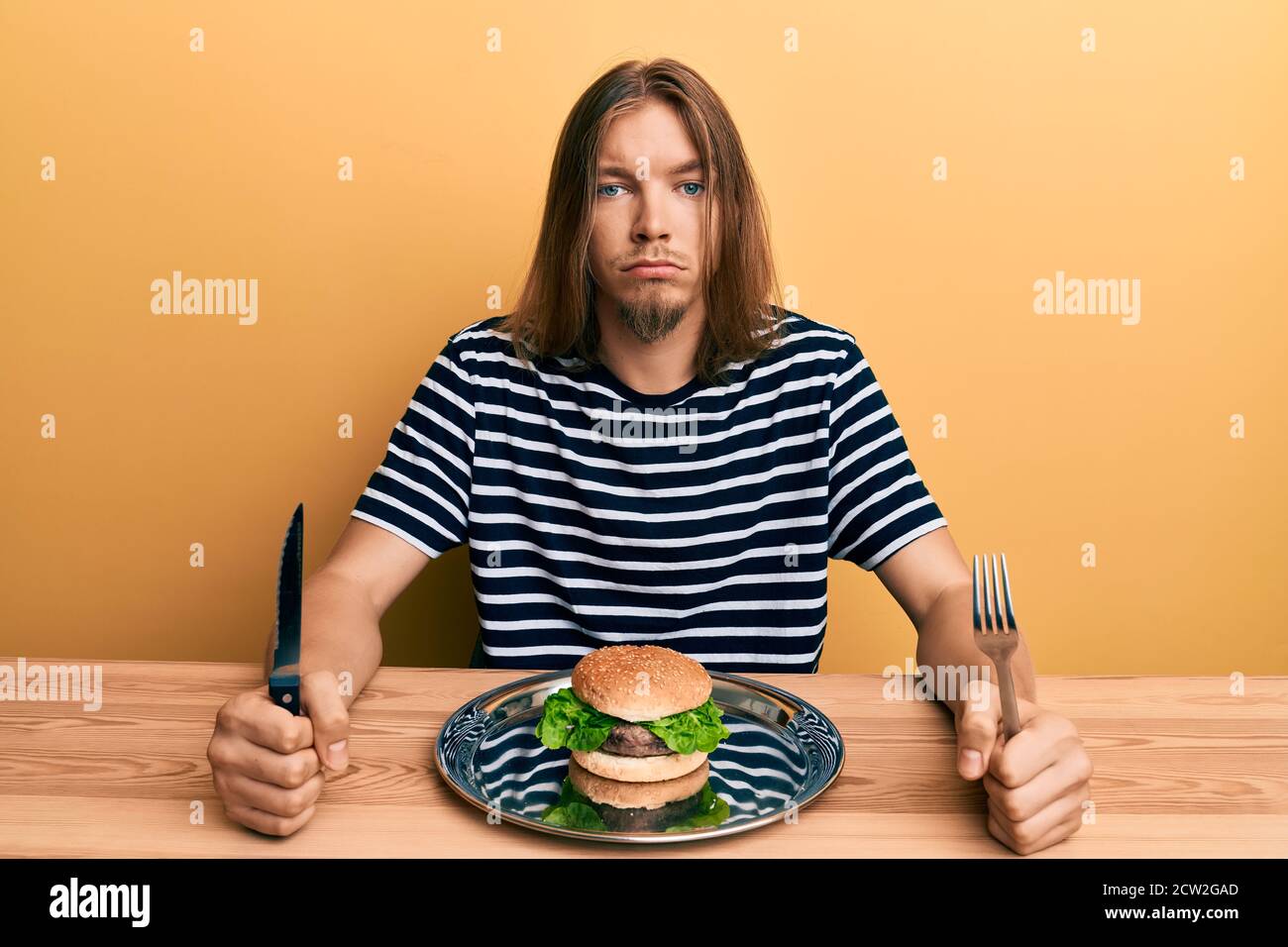 Handsome caucasian man with long hair eating a tasty classic burger ...