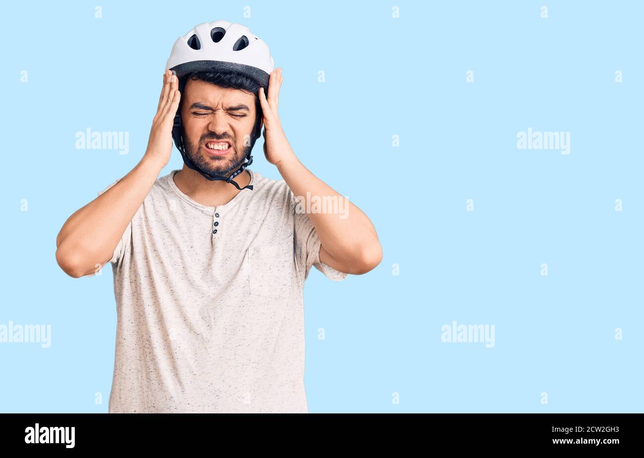 Young hispanic man wearing bike helmet suffering from headache ...