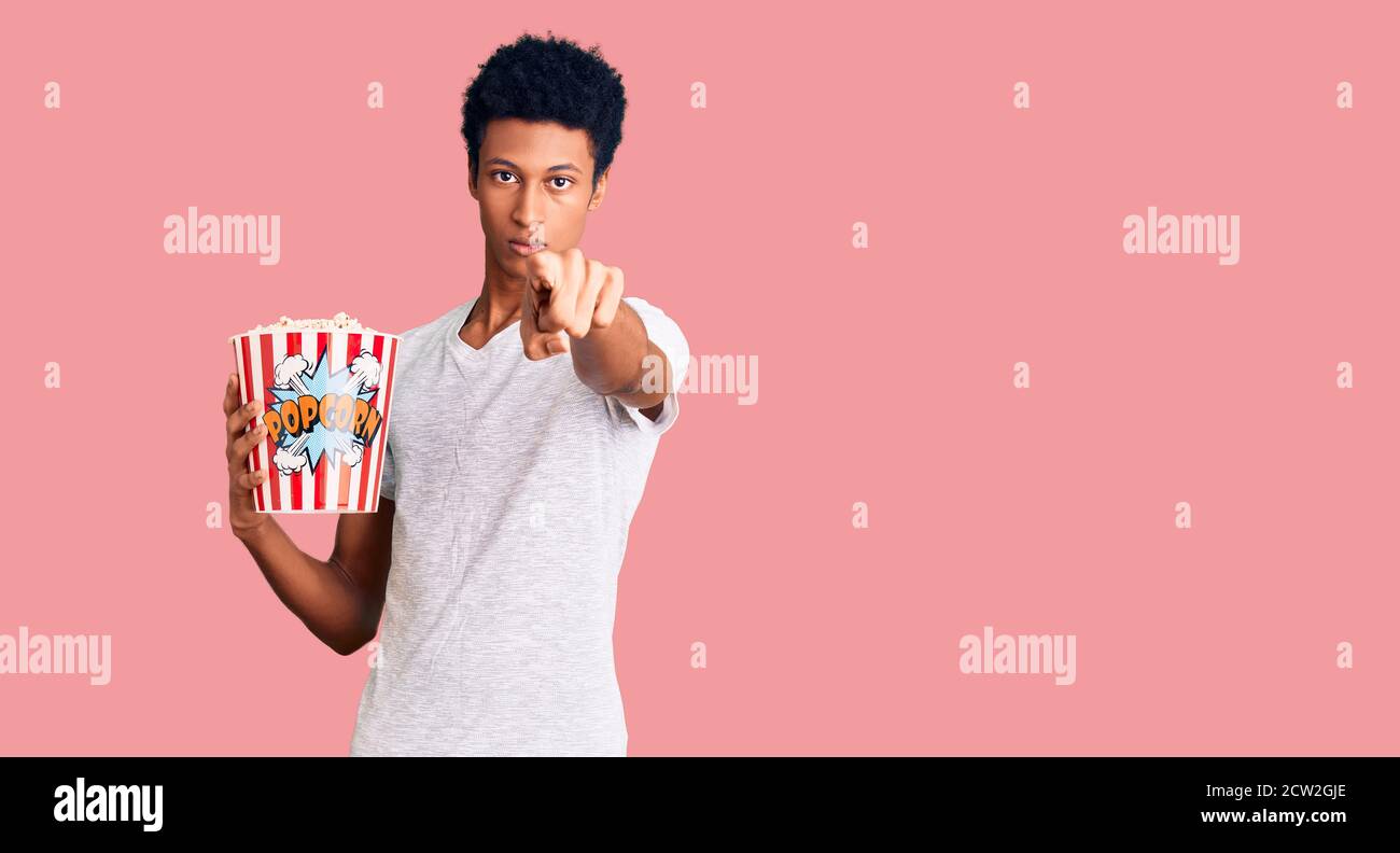 Young african american man holding popcorn pointing with finger to the camera and to you ...