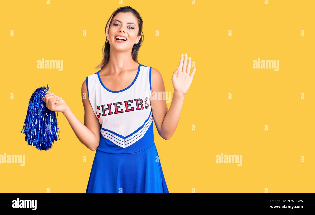 Young beautiful woman wearing cheerleader uniform waiving saying hello ...