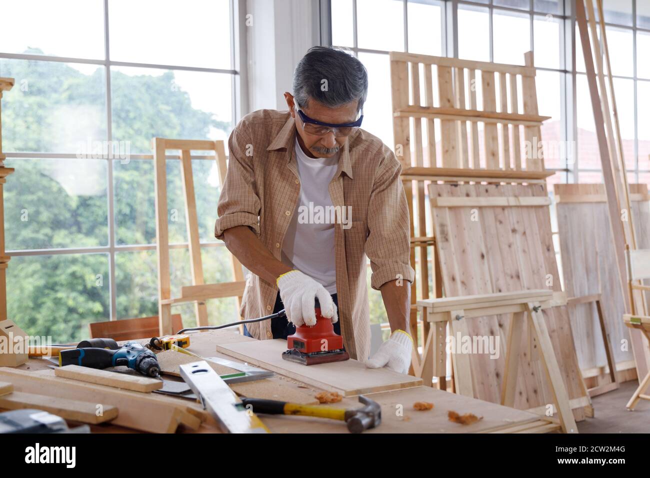 Senior man use red electric planer to smooth surface of wooden board in ...