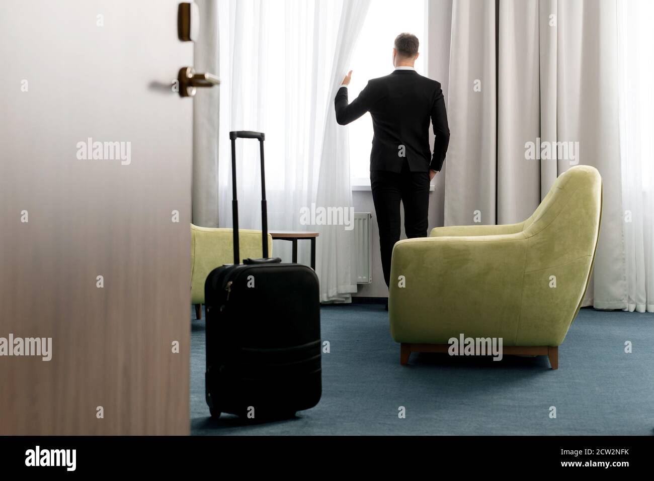 Rear view of businessman wearing dark suit standing in hotel room ...