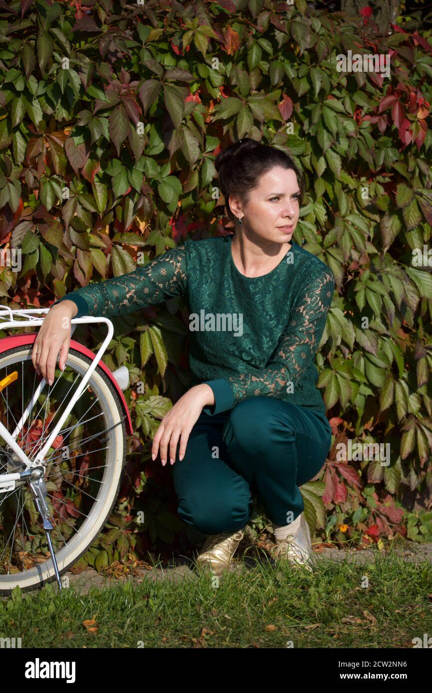 Portrait of a girl in a green tracksuit. Crouched by the bike against ...