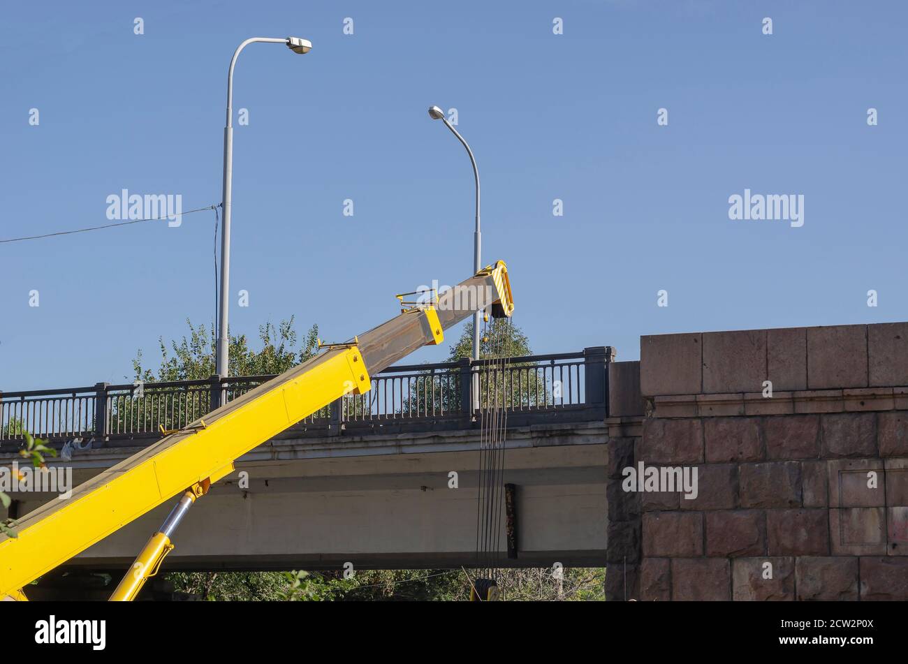 A mobile crane performs cargo work on a road bridge. Yellow crane boom ...