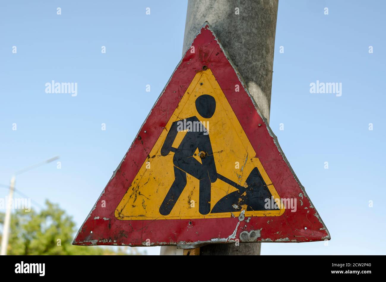 Road works warning sign. A road sign on a concrete post. Old dirty sign with scratches and dents ...