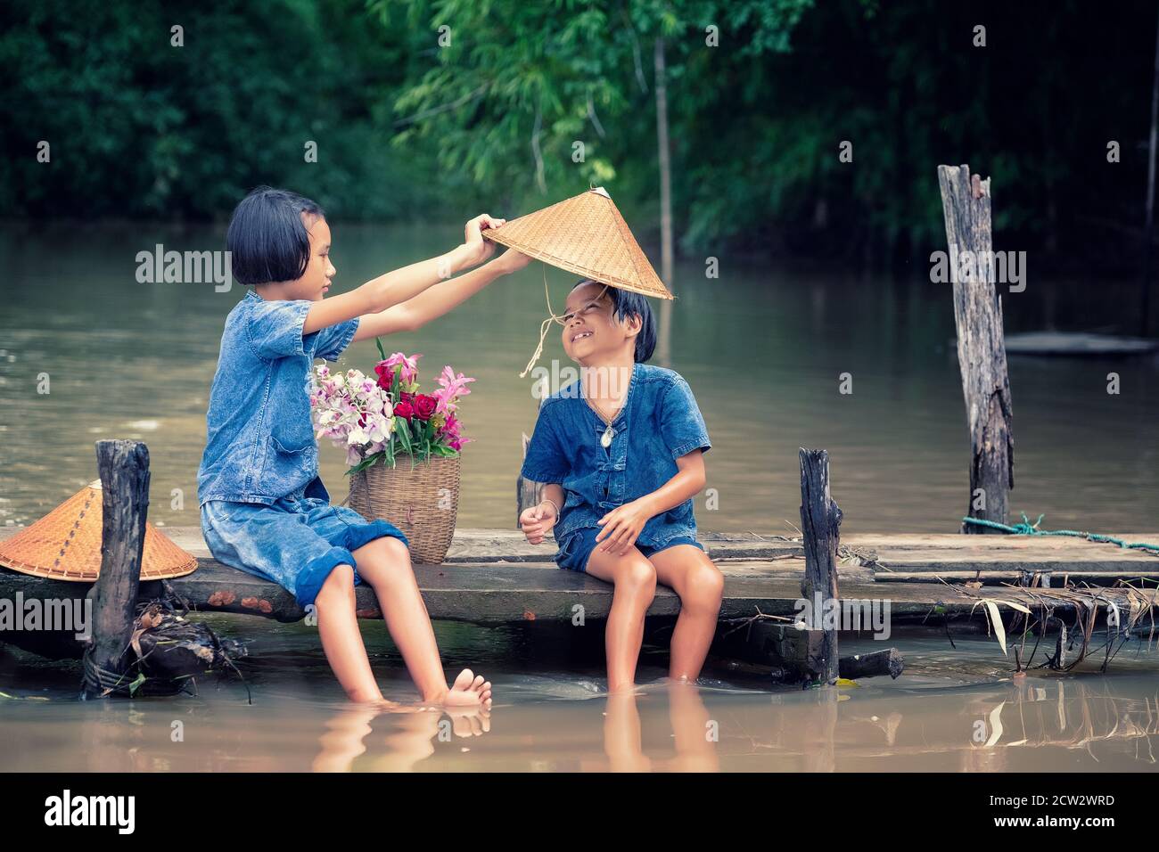 Two girl children sitting and playing water together on wooden bridge ...