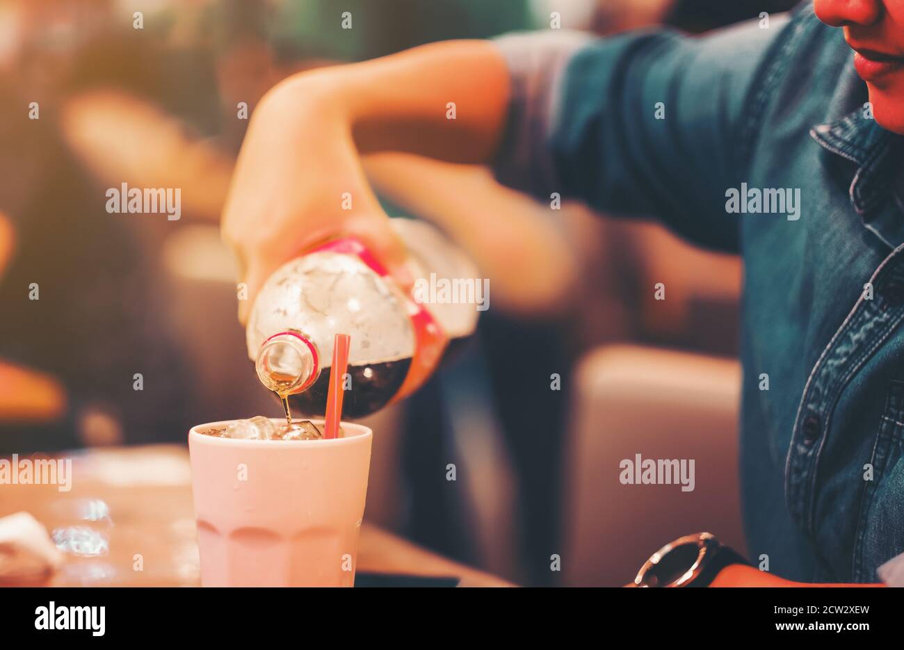 Woman hand hold pour cola in glass of cola splashing with ice on wooden ...