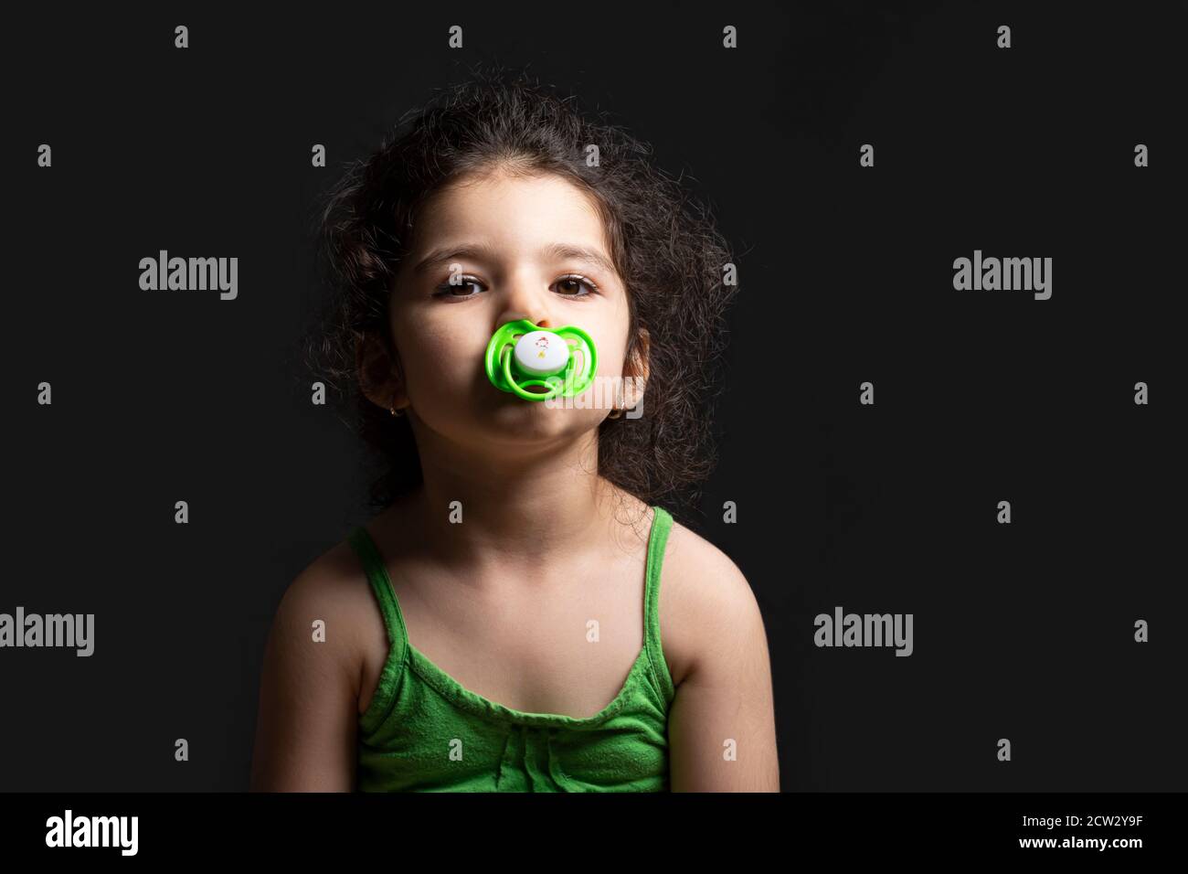 Close-up portrait of a three years old girl with pacifier and green ...