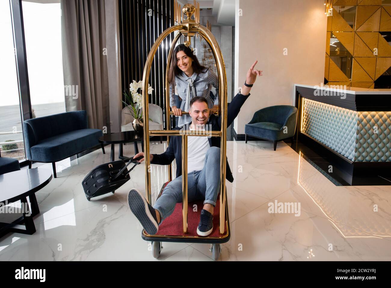 Young happy couple have fun pushing hotel luggage cart in hotel hall ...