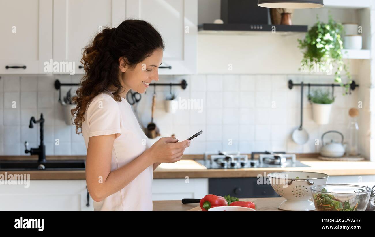 Happy young woman texting on cellphone cooking at home Stock Photo - Alamy
