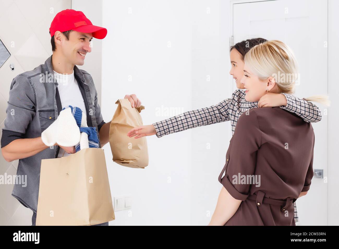 Smiling young woman and her daughter receiving food delivery from ...