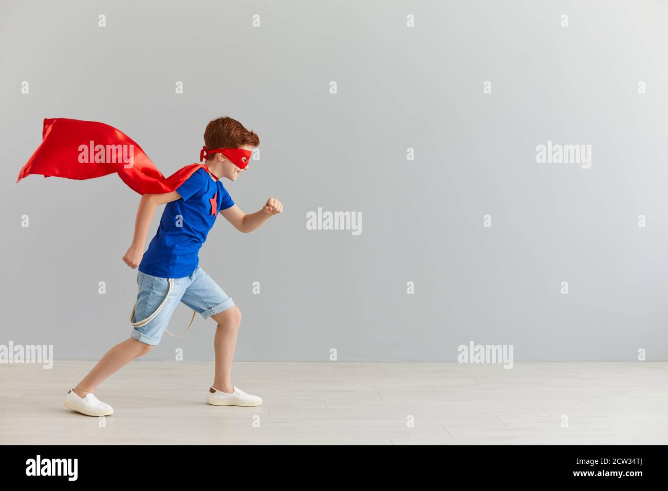 Little boy in a superhero costume running on a background of a gray ...