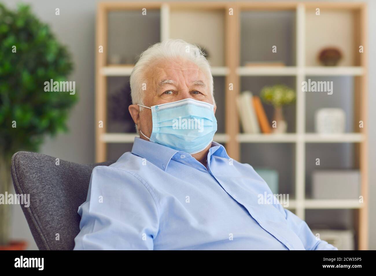 Serious senior citizen wearing medical face mask sitting in armchair ...