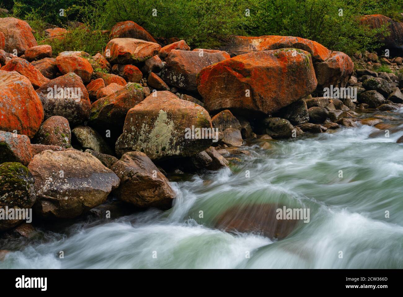 A red rock creek with rapid currents in valley of mountains in Sichuan ...