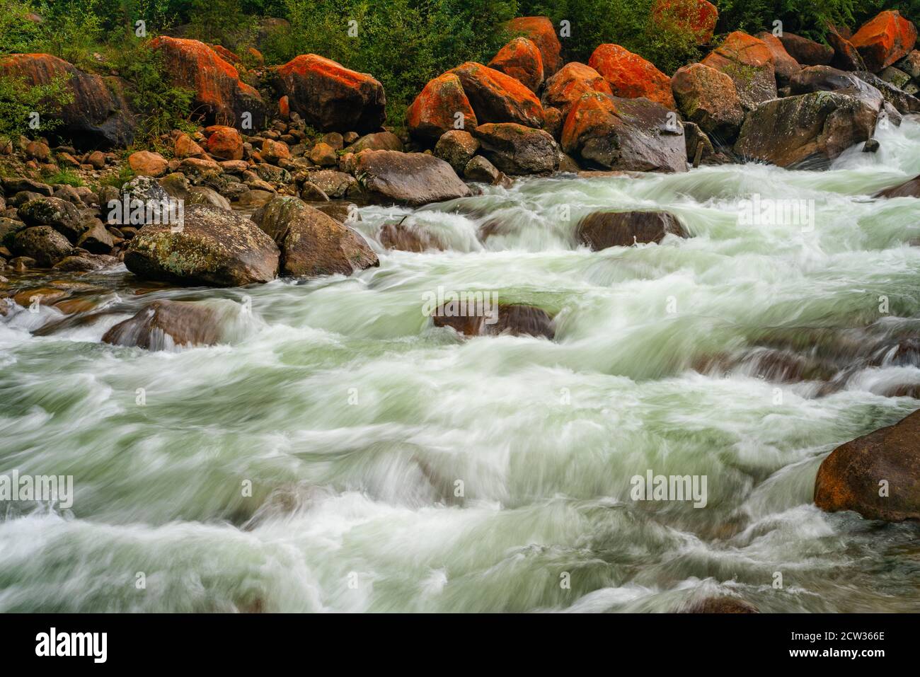 A red rock creek with rapid currents in valley of mountains in Sichuan ...