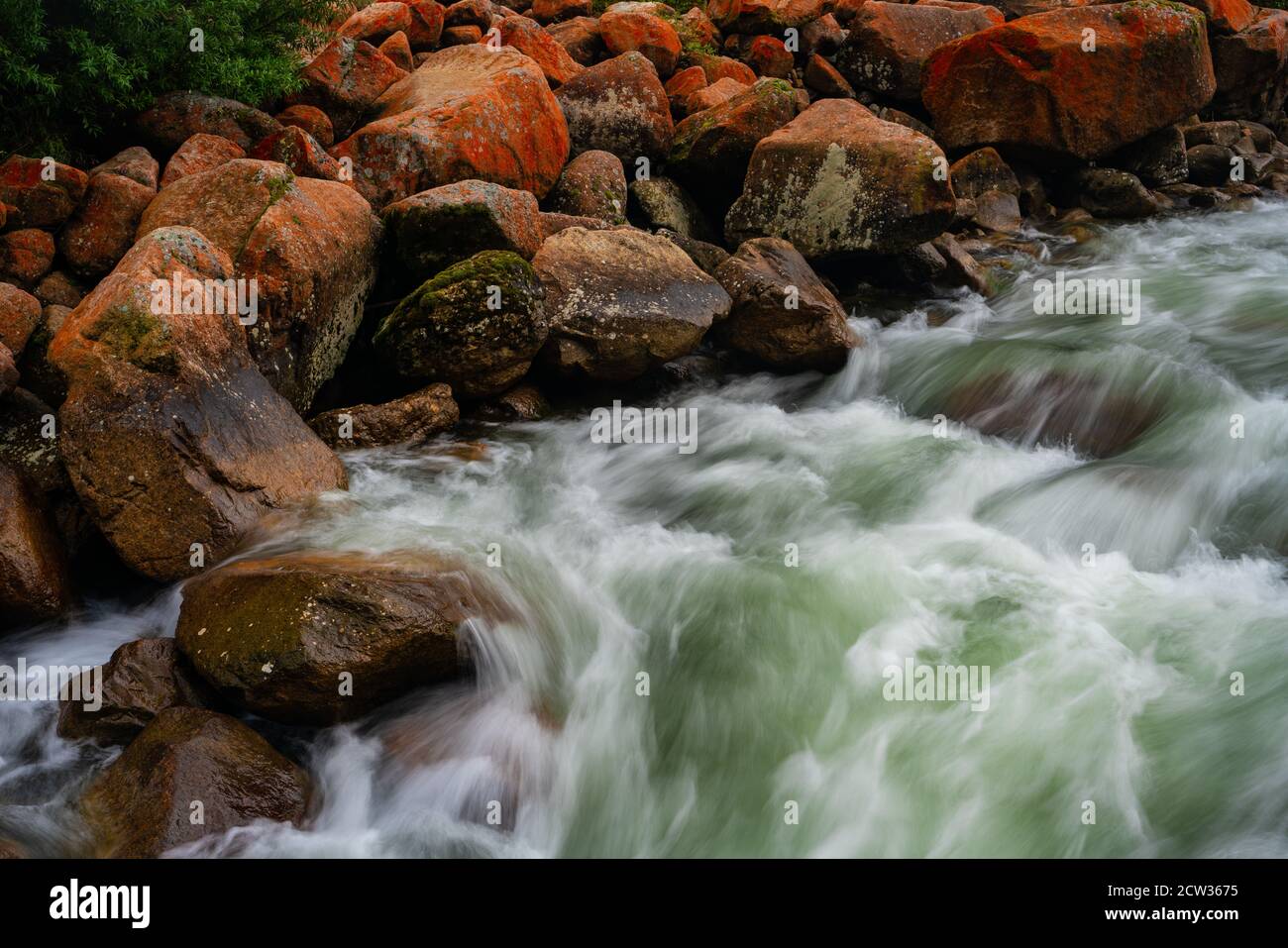 A red rock creek with rapid currents in valley of mountains in Sichuan ...