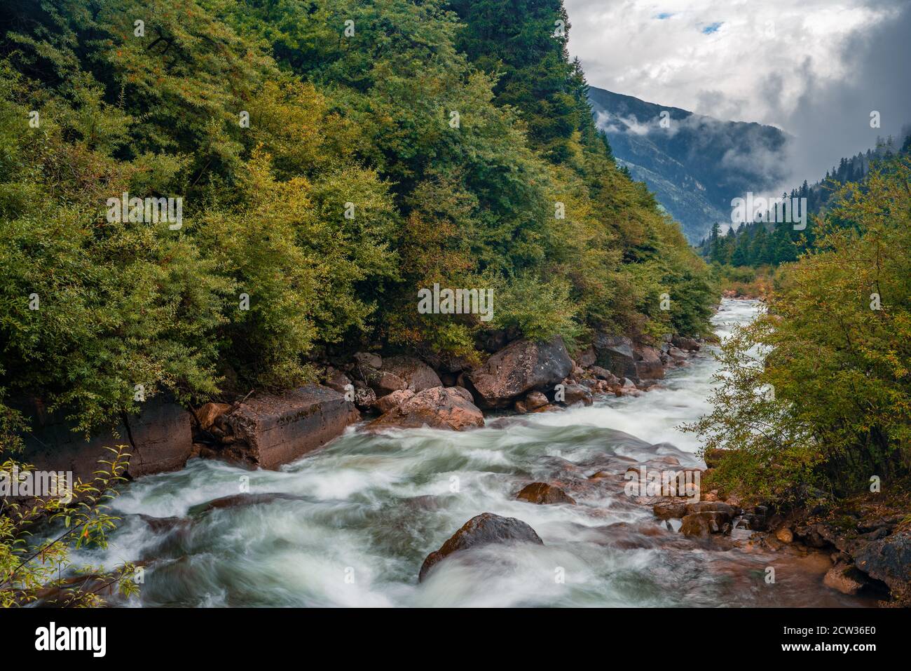 A red rock creek with rapid currents in valley of mountains in Sichuan ...
