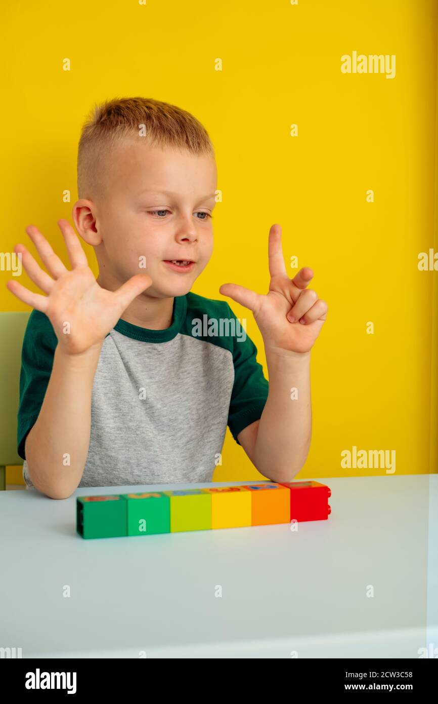 boy counting on his finger.on the table colored figures blocks.On a ...