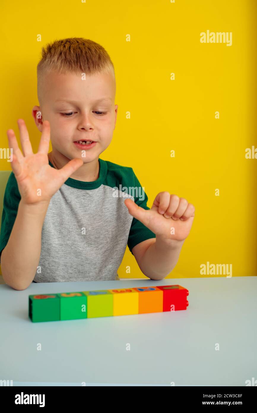 boy counting on his finger.on the table colored figures blocks.On a ...