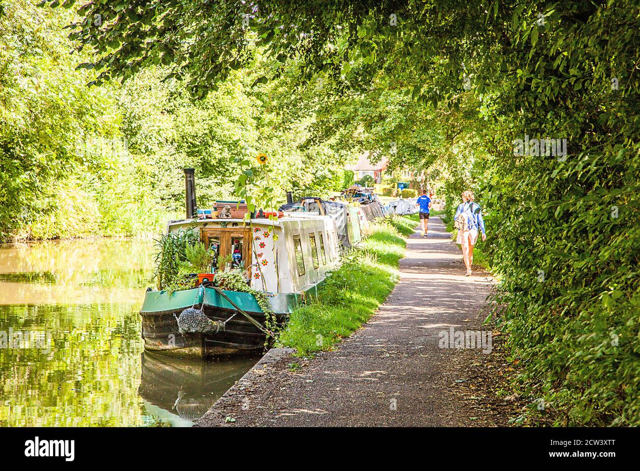 Woman walking along the towpath past canal narrowboats on the Grand ...