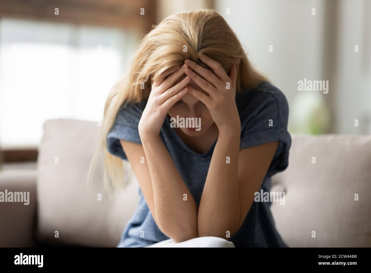 Depressed young lady sitting on couch hugging head with hands Stock ...