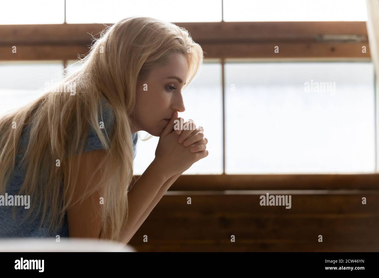 Sad young female leaning forward propping chin on clasped hands Stock ...