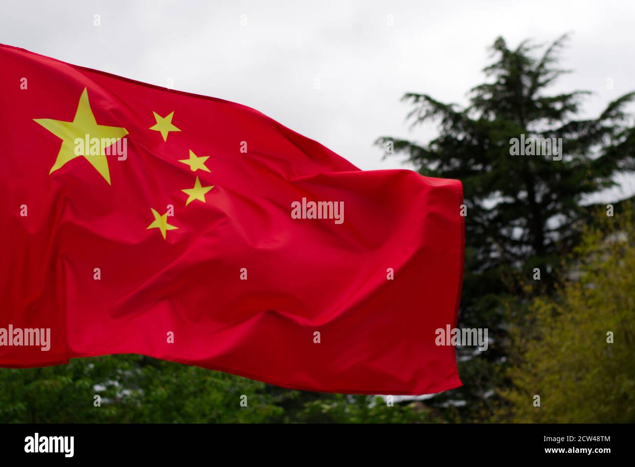 Chinese flag waving in the wind. Background with trees and sky out of ...