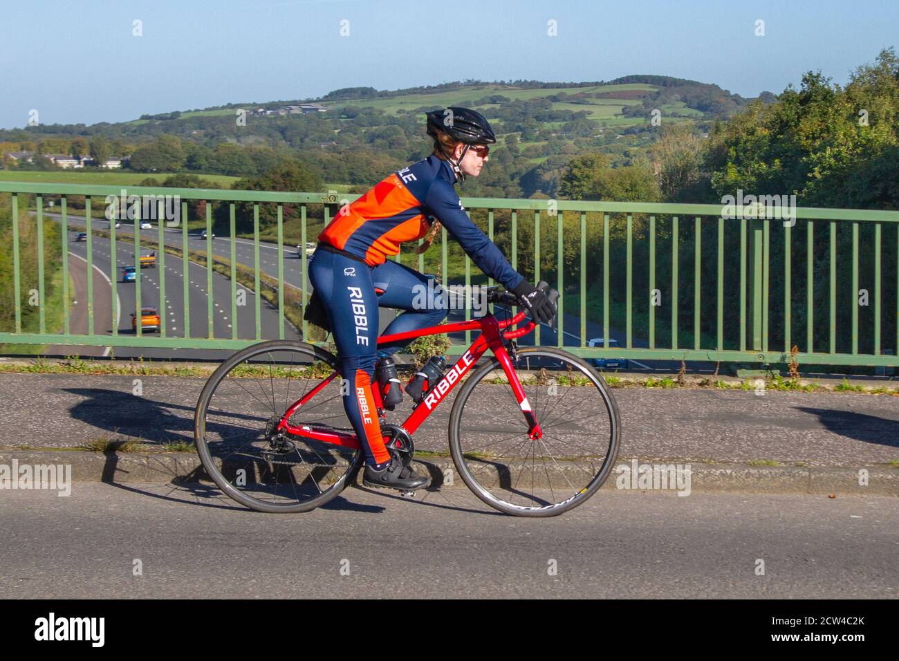 Woman cyclist riding red Ribble road bike on countryside route crossing ...