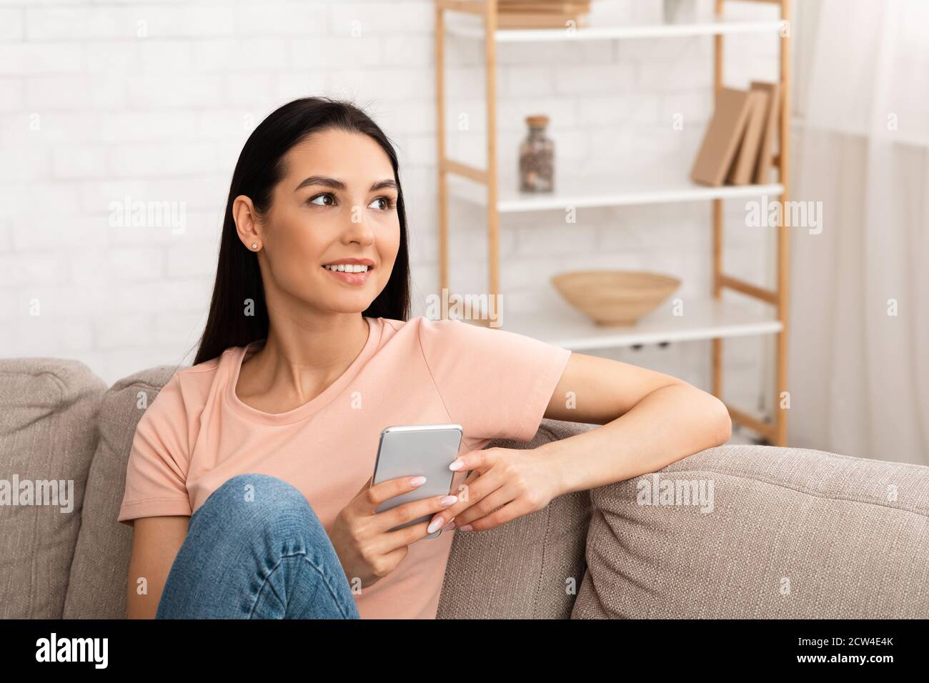 Distracted woman holding mobile phone sitting on the couch Stock Photo ...