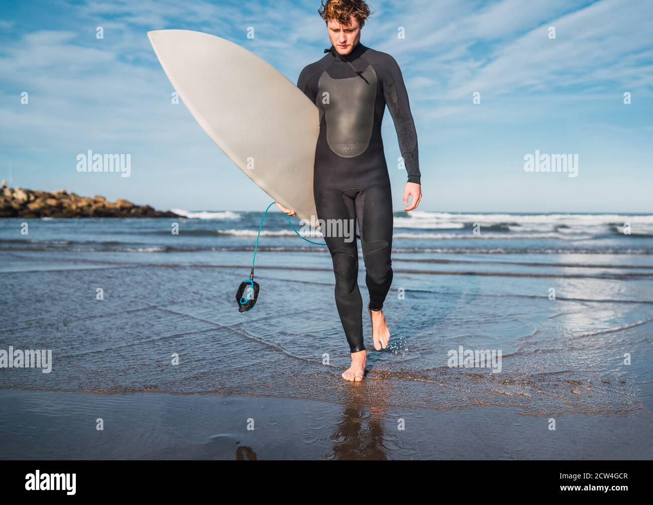 Portrait of young surfer leaving the water with surfboard under his arm ...
