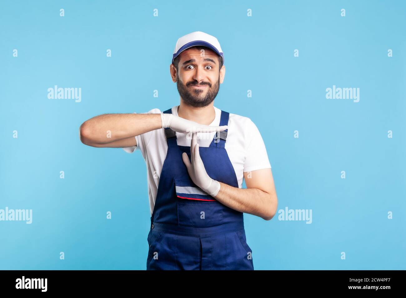 Overworked handyman in overalls and gloves showing time out gesture ...