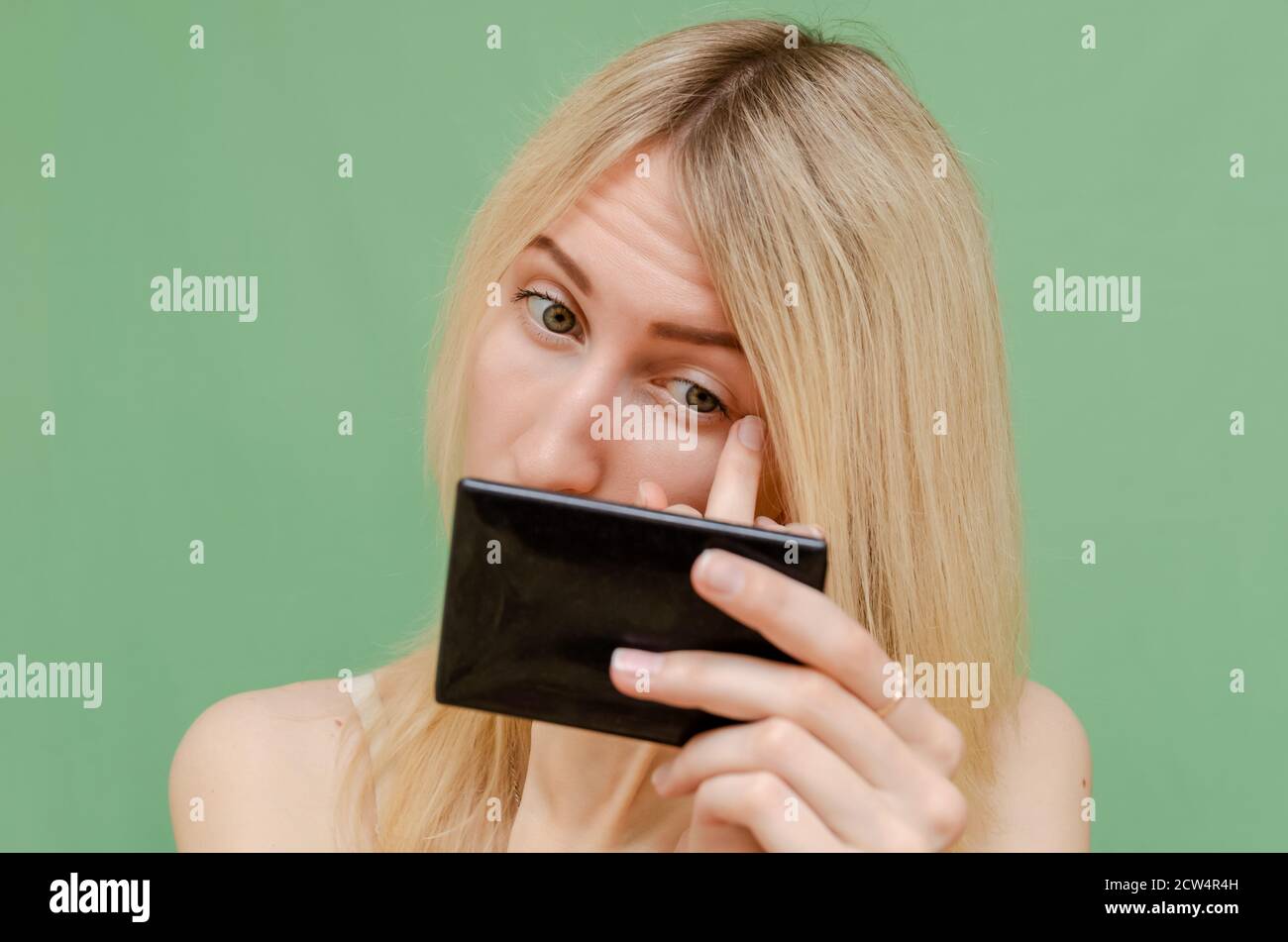 a young woman looks in a mirror and uses a concealer to smooth out acne ...