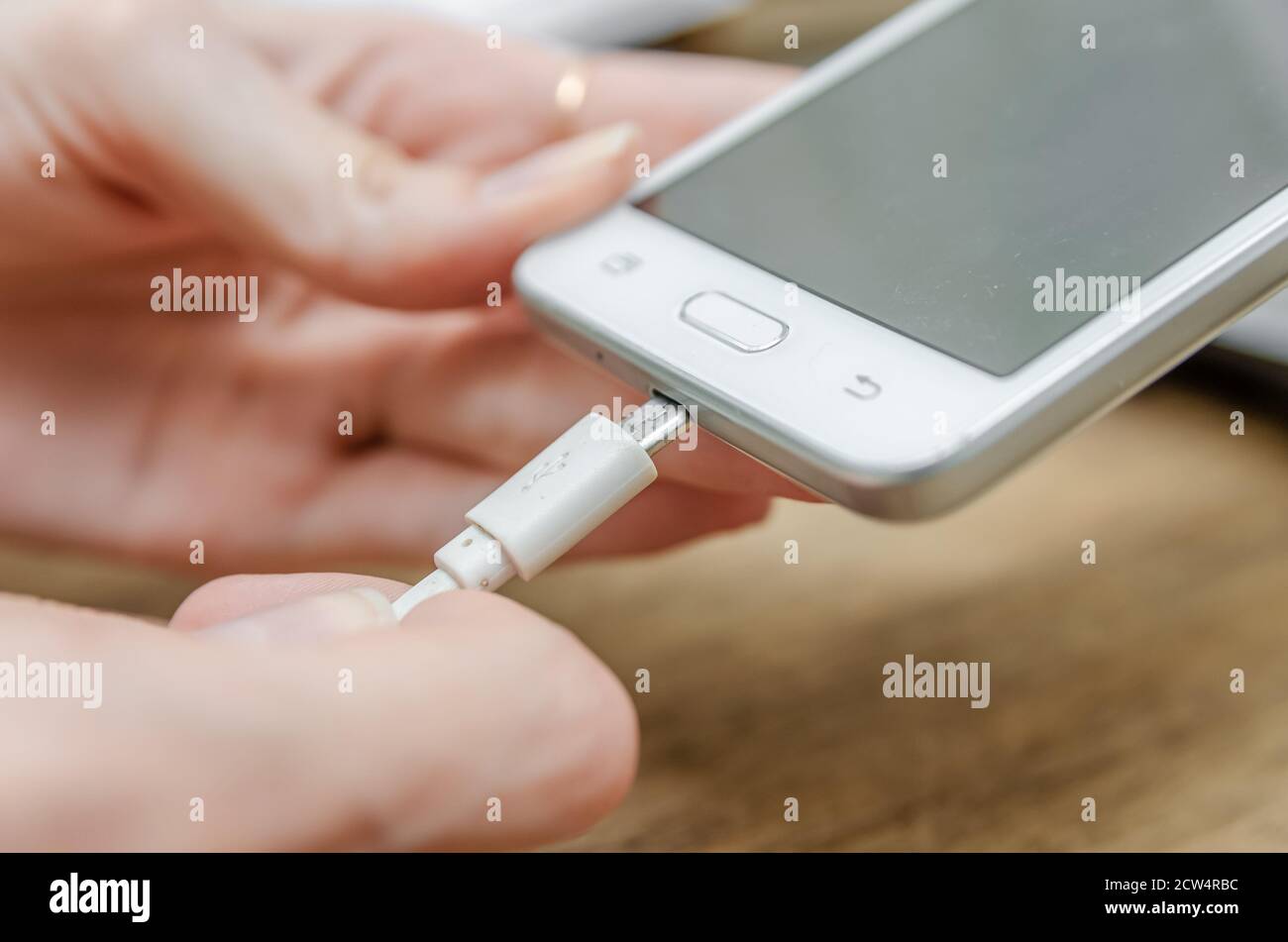 Female hand connecting a white lightning charging cable to a white ...