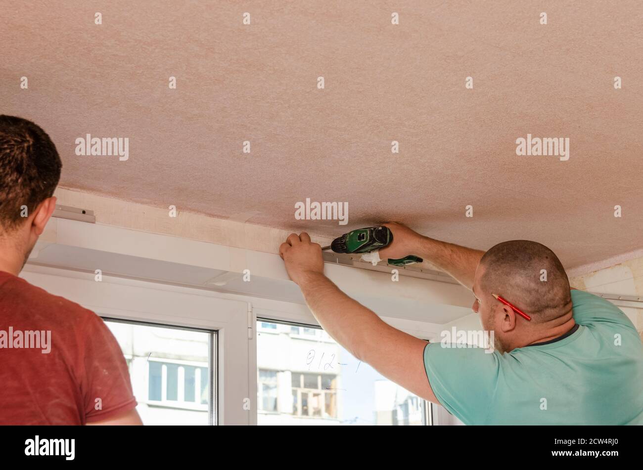 2 men fix the metal frame for the stretch ceiling with an electric ...