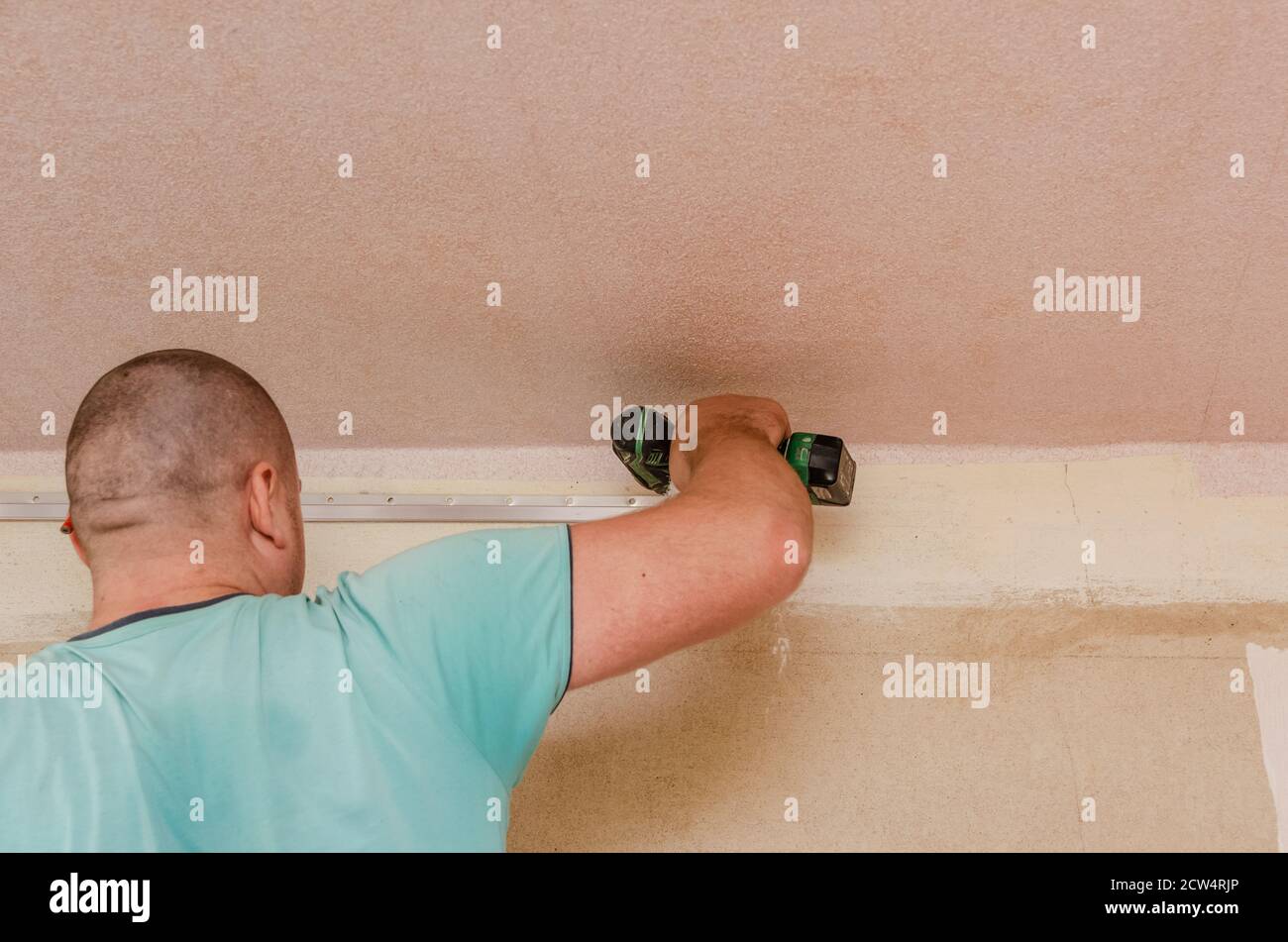 A young man fixing a metal frame for a stretch ceiling with an electric ...