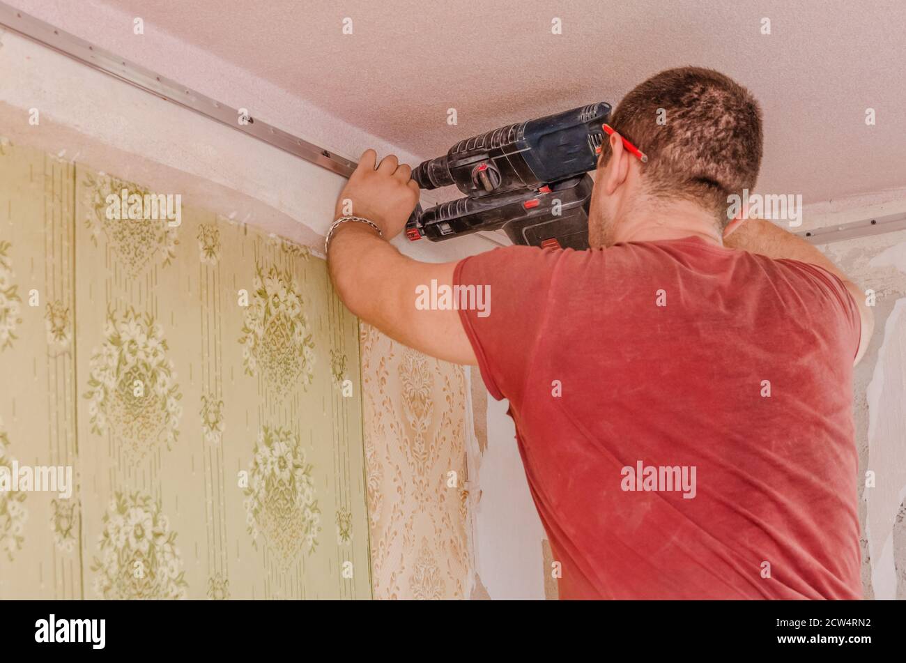 A young man fixing a metal frame for a stretch ceiling with an electric ...