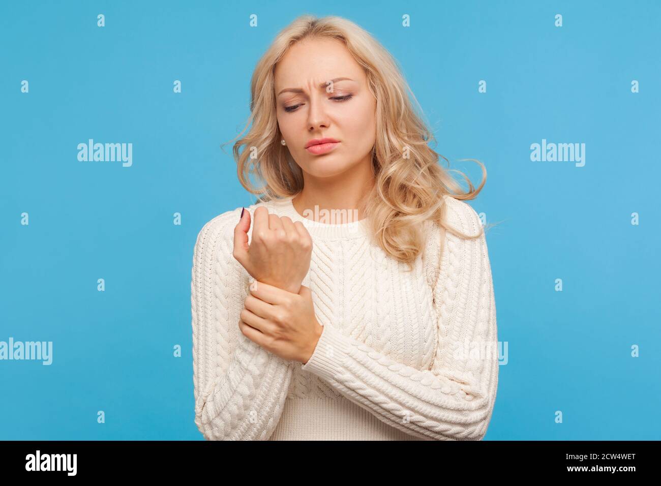 Sad woman with curly blond hair massaging her wrist, numbness, muscle ...