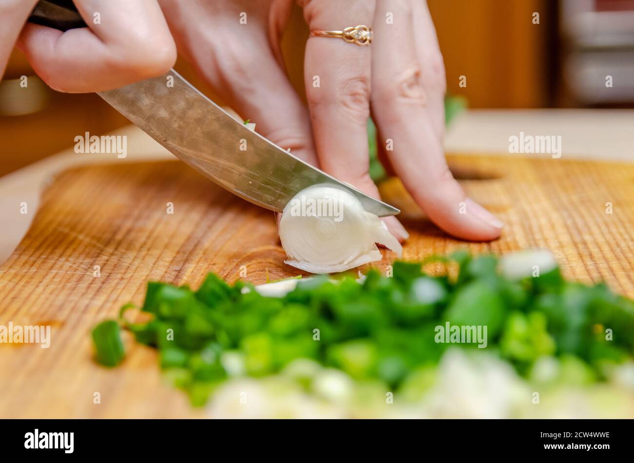 Female hands chopping green onion with a knife on a wooden board ...