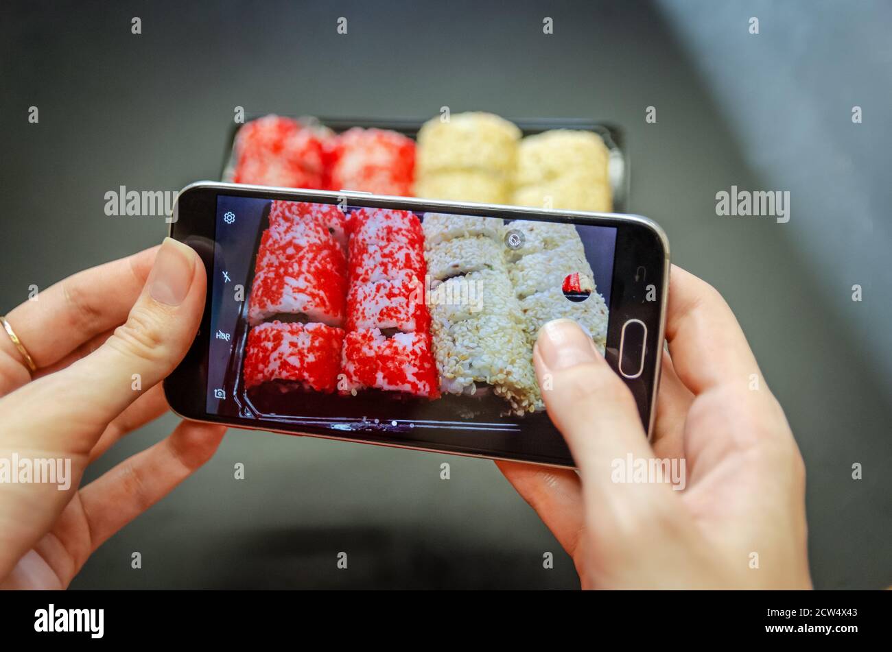 A girl photographs red and white sushi on the phone from different ...