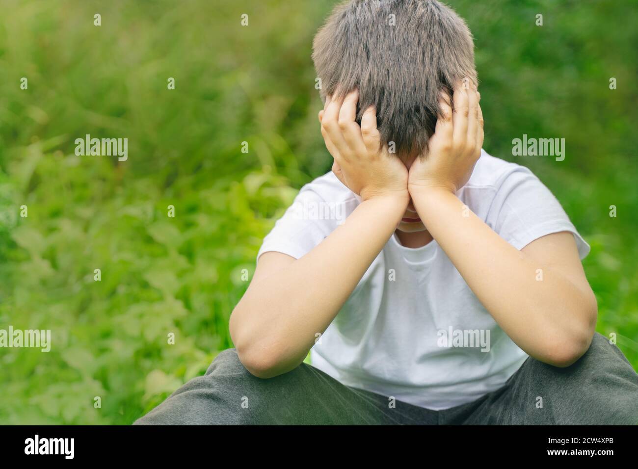 unhappy child covering her face with hands. crying boy sitting alone in ...