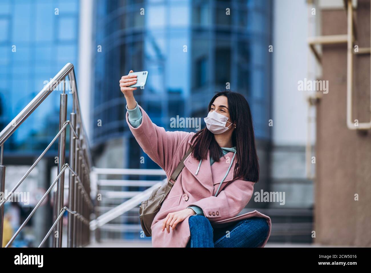 Female in medical protective mask outdoors using smart phone. Health ...