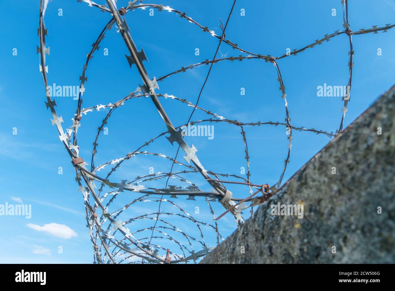 Barbed wire coiled around a fence against a blue sky Stock Photo - Alamy