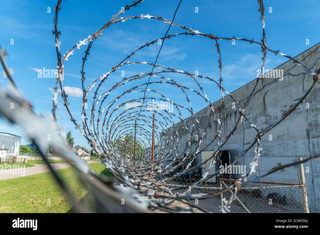 Barbed wire coiled around a fence against a blue sky Stock Photo - Alamy