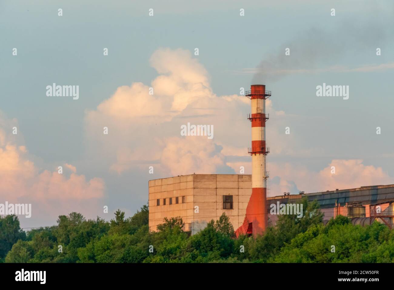 factory pipe with smoke against a background of pink sunset and green ...