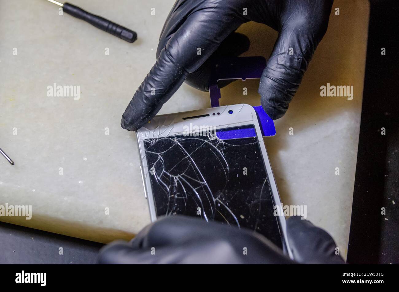 Specialist replaces a cracked screen on a white smartphone close-up ...
