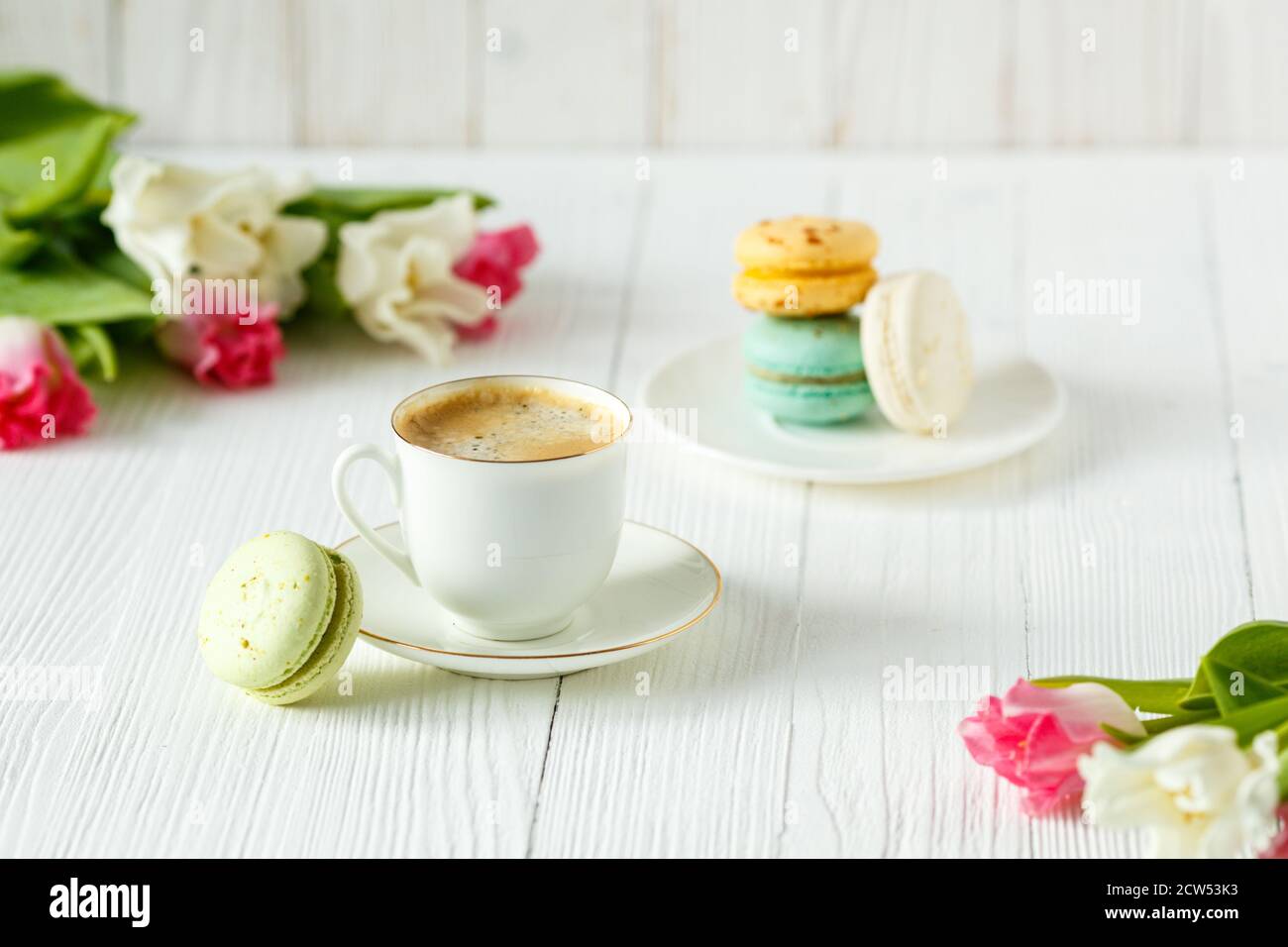 Coffee, pink and white tulips and macarons on the white wooden table ...