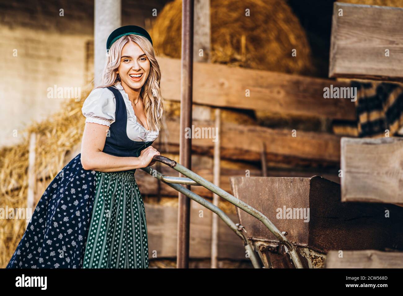 Pretty smiling blonde in traditional dress with wheelbarrow working in ...