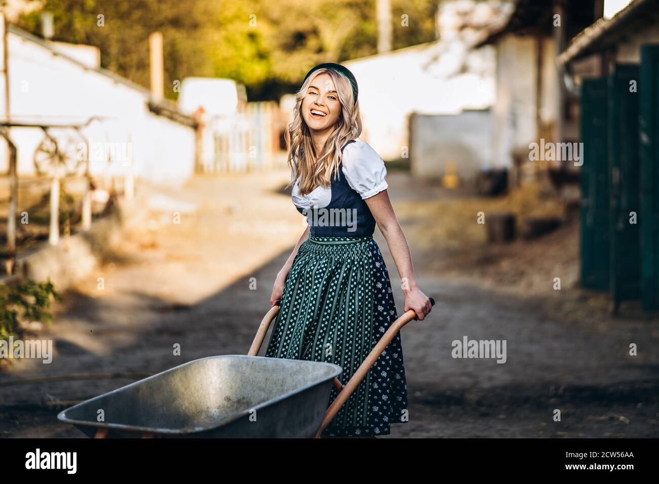 Pretty smiling blonde in traditional dress with wheelbarrow working in ...
